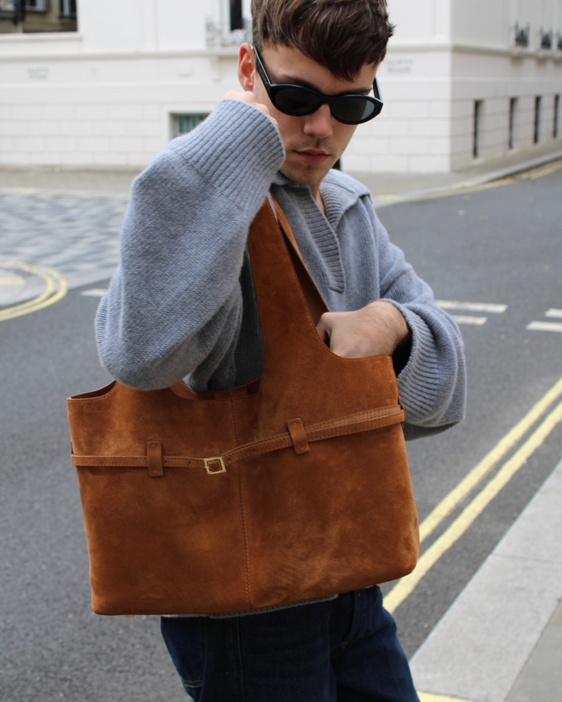 Stylish individual showcasing a brown suede Manu Atelier tote bag%2C paired with a cozy grey oversized sweater and dark jeans in an urban setting