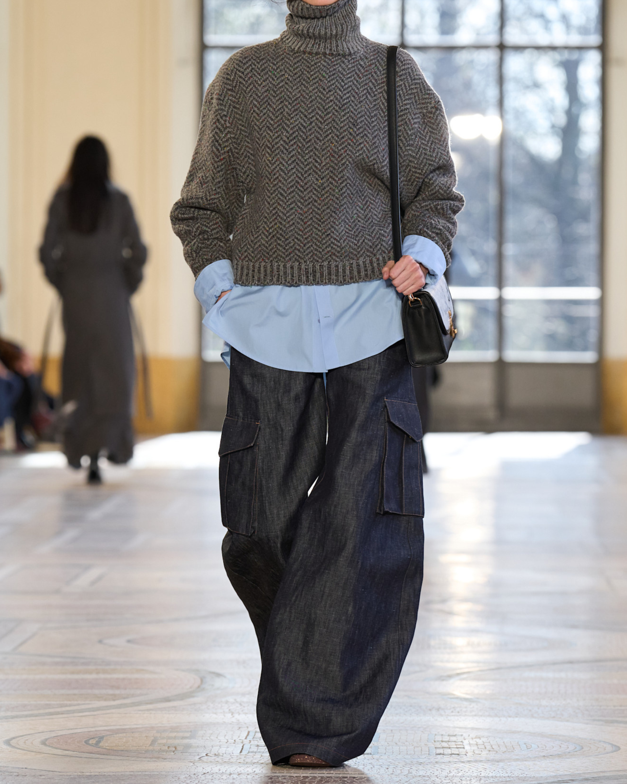 Gabriela Hearst fall 2026 look featuring a gray herringbone turtleneck sweater layered over a light blue shirt with wide-leg dark denim cargo pants and a black shoulder bag