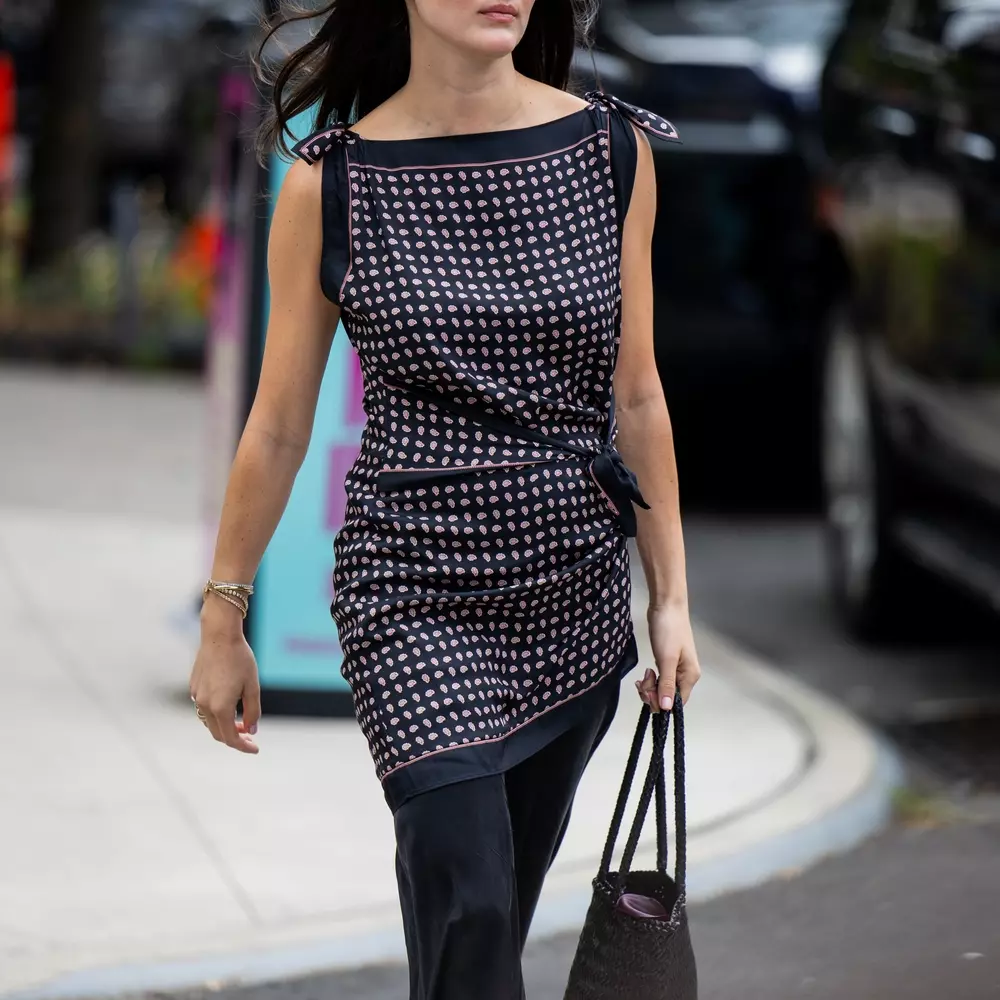 Elegant outfit featuring a navy polka dot dress layered over black pants, paired with chic sunglasses and a woven black handbag