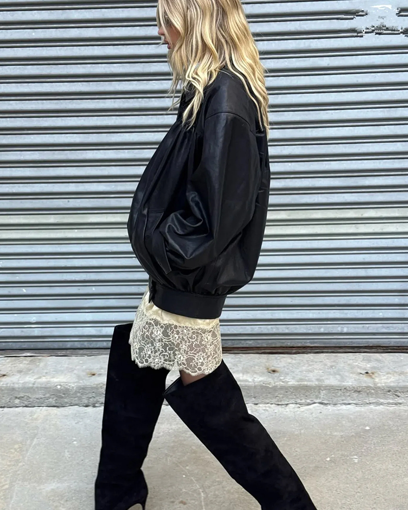 Street style look featuring a black leather bomber jacket over a lace mini skirt with knee-high suede boots%2C styled against an industrial metal shutter backdrop