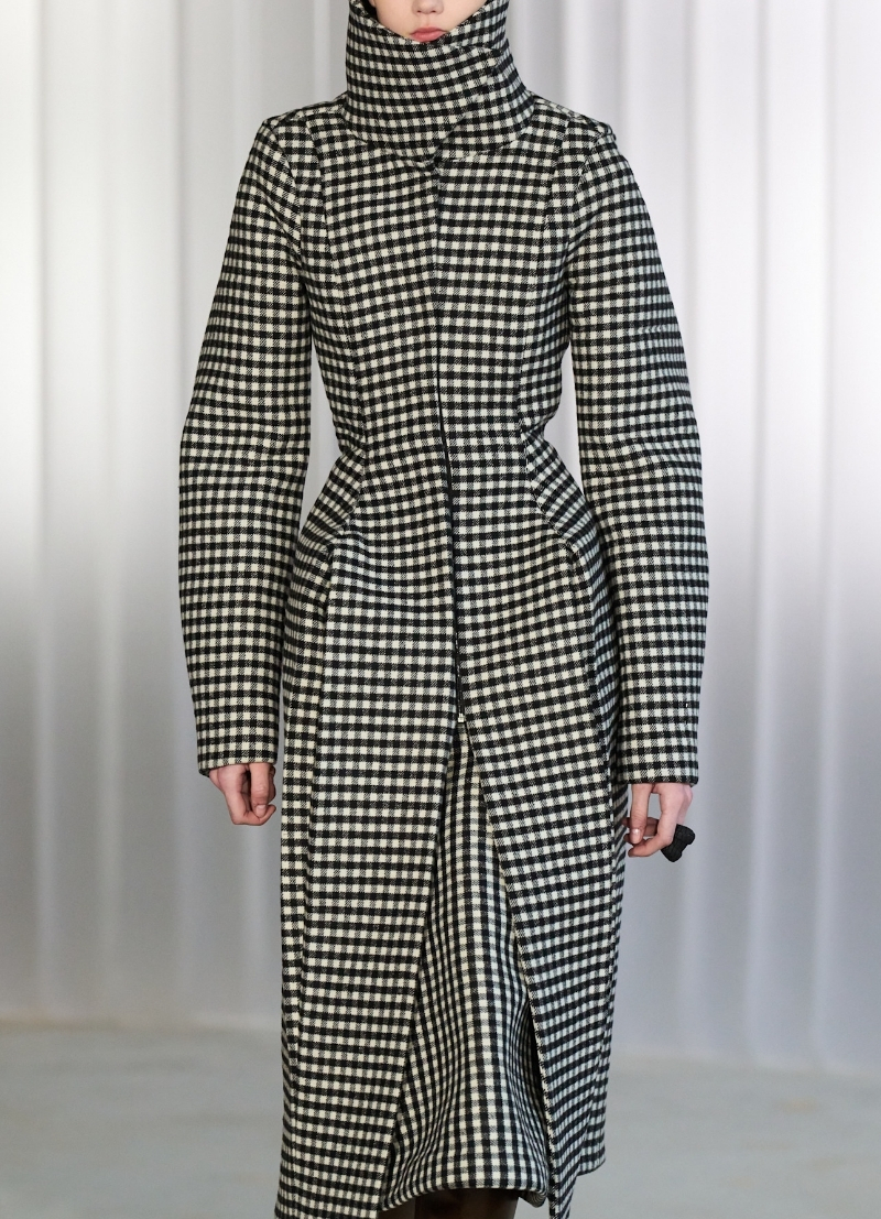 Black and white checked long coat with fitted waist and high funnel collar presented on the runway