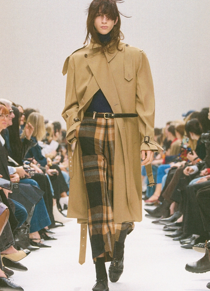 Camel trench coat layered over plaid trousers with a black belt and boots on the runway
