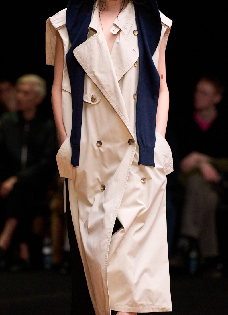 Sleeveless cream trench coat with double-breasted buttons and navy scarf detail on the runway