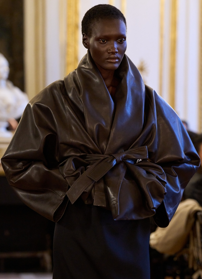 Oversized dark brown leather wrap jacket with sculptural sleeves and a tied waist on the runway