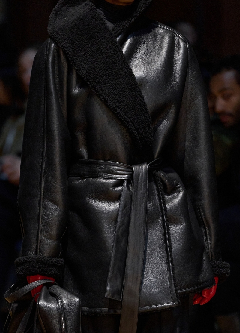 Black leather shearling wrap coat with belted waist and red gloves styled on the runway