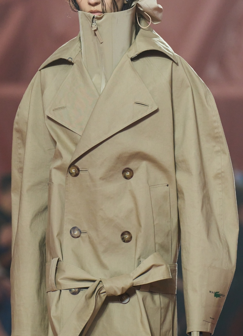 Beige double-breasted trench coat with high zip collar and belted waist presented on the runway