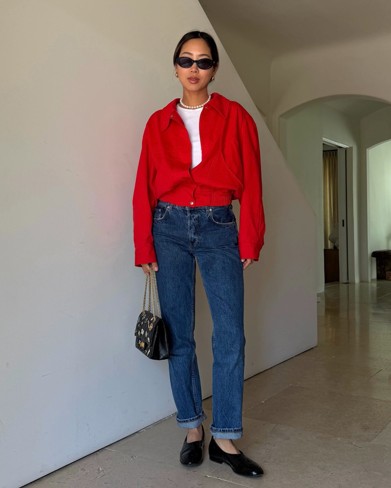 Red cropped jacket layered over a white tee with straight-leg jeans%2C black ballet flats%2C and shoulder bag in a minimalist hallway%0A