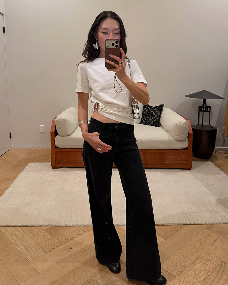Mirror selfie outfit with white T-shirt%2C black wide-leg jeans and leather boots%2C accessorized with mini shoulder bag in cozy living room setting
