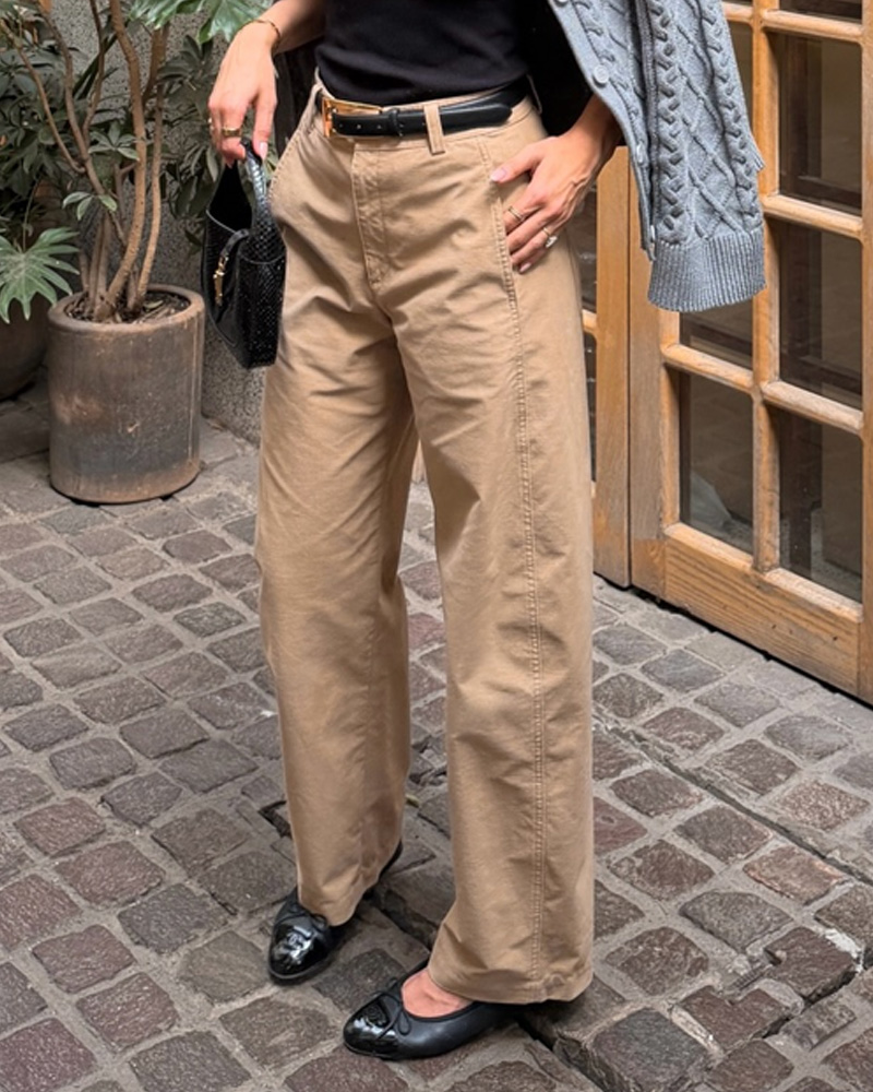 High-waisted beige wide-leg trousers styled with black top%2C leather belt and ballet flats on cobblestone street