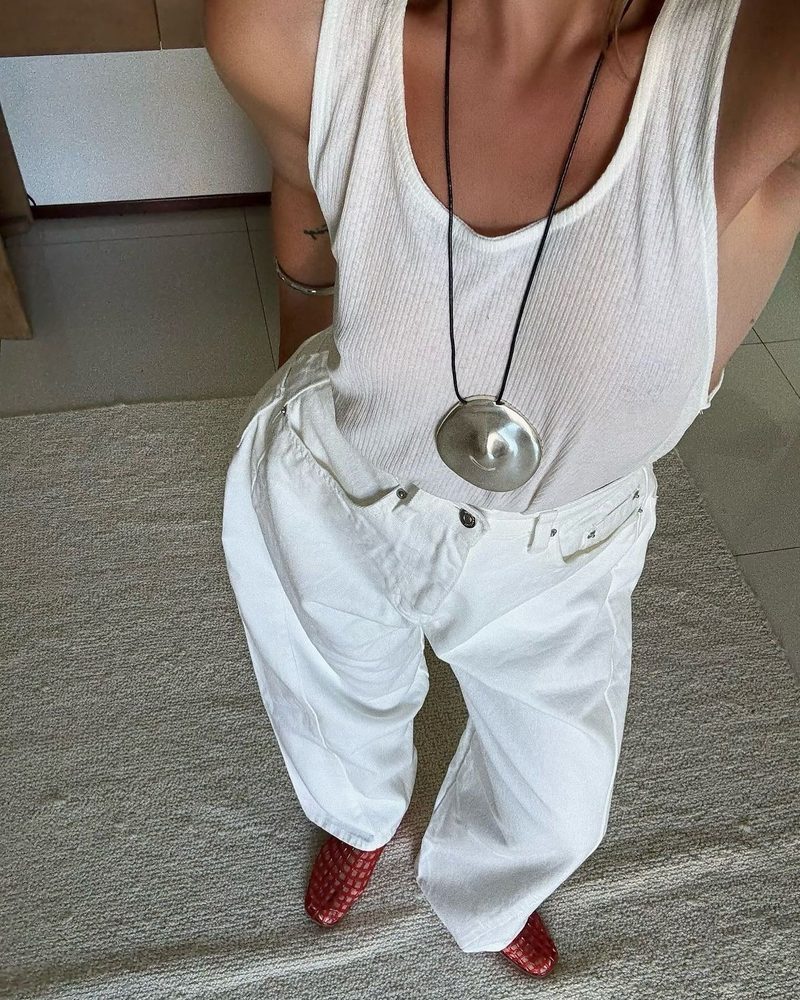 Stylish outfit featuring white wide-leg jeans paired with a ribbed white tank top and statement silver pendant necklace%2C complemented by vibrant red croc-embossed heels