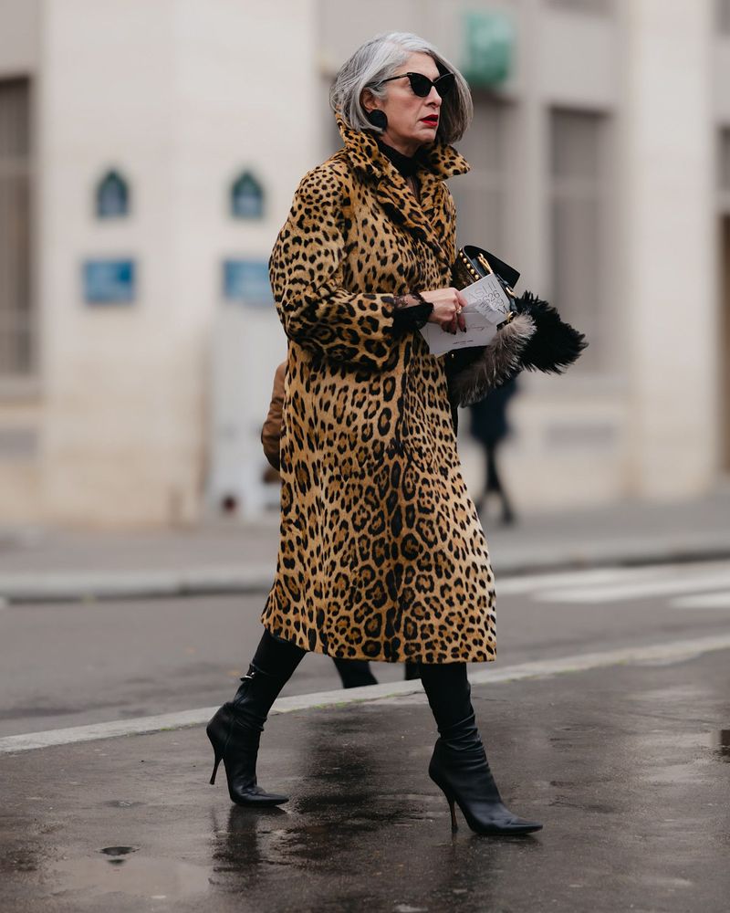 Woman wearing a leopard print faux fur coat with black leather high-heeled boots and cat-eye sunglasses walking on a city street