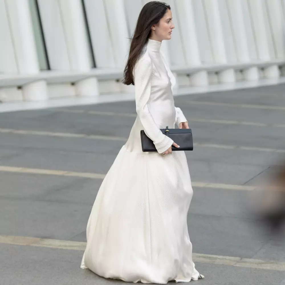 Elegant white maxi dress with a high neckline and flared skirt, complemented by a sleek black clutch, capturing a modern autumn look.