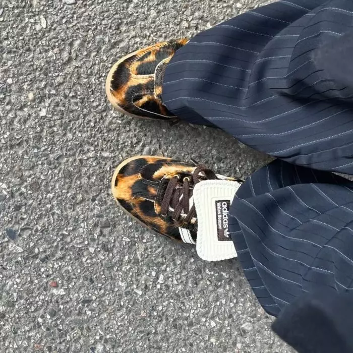 Adidas sneakers with a leopard-print design, paired with stylish pinstriped trousers, set against a textured pavement backdrop