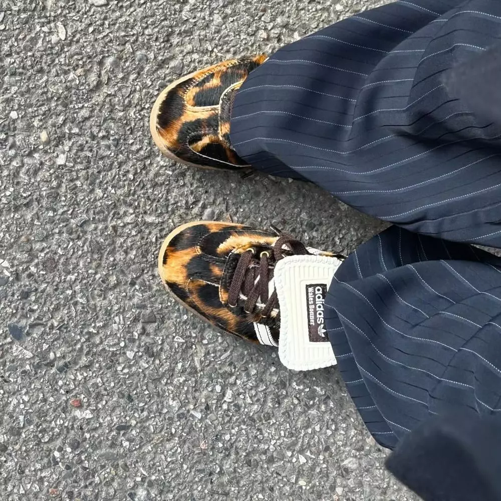 Adidas sneakers with a leopard-print design, paired with stylish pinstriped trousers, set against a textured pavement backdrop