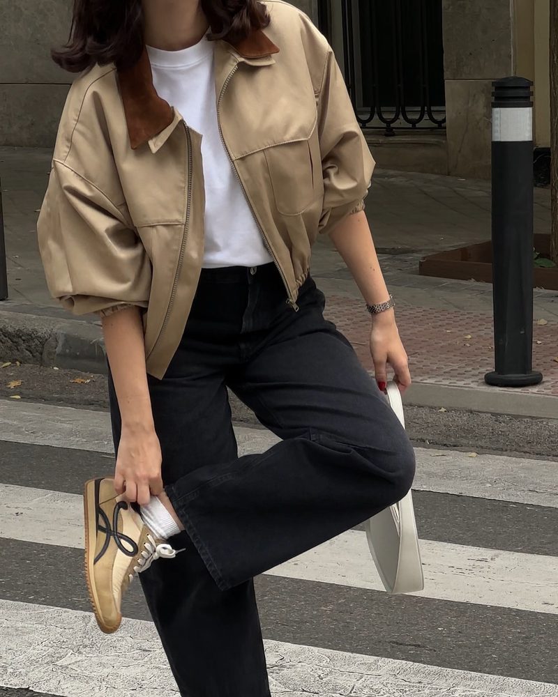 Casual street style showcases a model in a beige bomber jacket with brown collar%2C paired with black wide-leg jeans and stylish beige sneakers.
