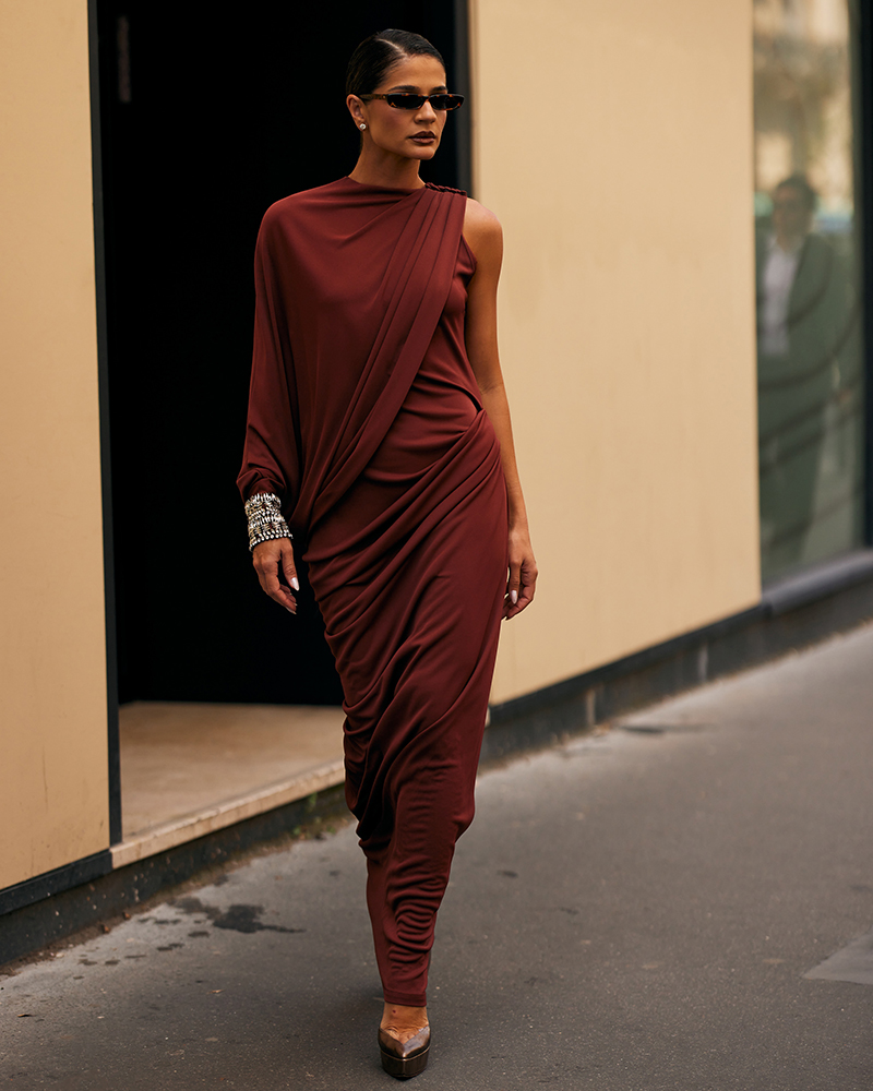 Burgundy draped one-shoulder maxi dress styled with stacked silver bracelets and sunglasses on a city street