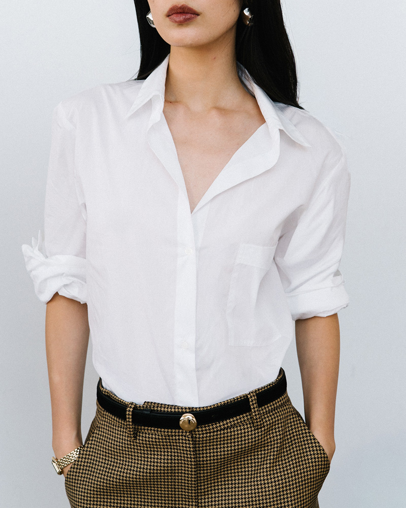 White button-down shirt with rolled sleeves styled with houndstooth trousers and a black velvet-trim belt against a white backdrop White button-down shirt with rolled sleeves styled with houndstooth trousers and a black velvet-trim belt against a white backdrop