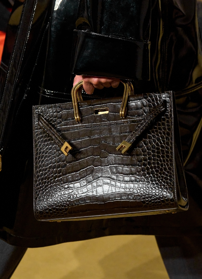 Tory Burch dark brown croc-embossed top-handle bag with gold hardware, carried with a glossy black runway coat