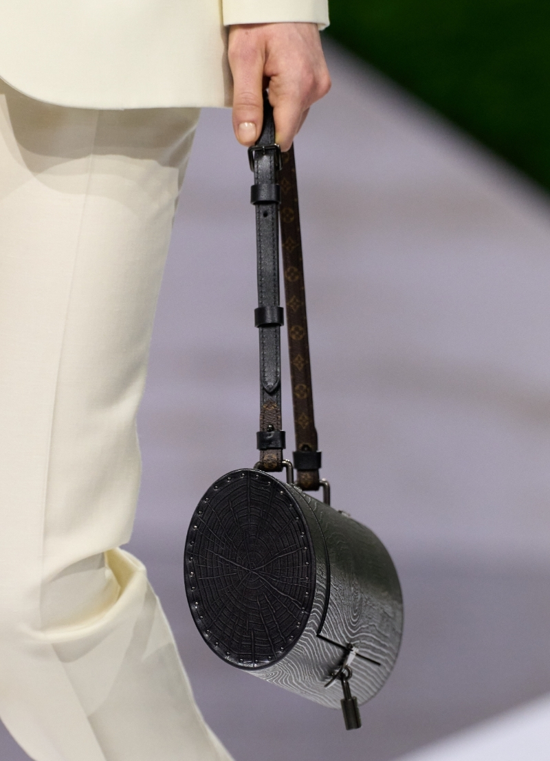 Louis Vuitton black cylindrical bag with wood-grain texture and monogram strap, carried with an ivory runway suit