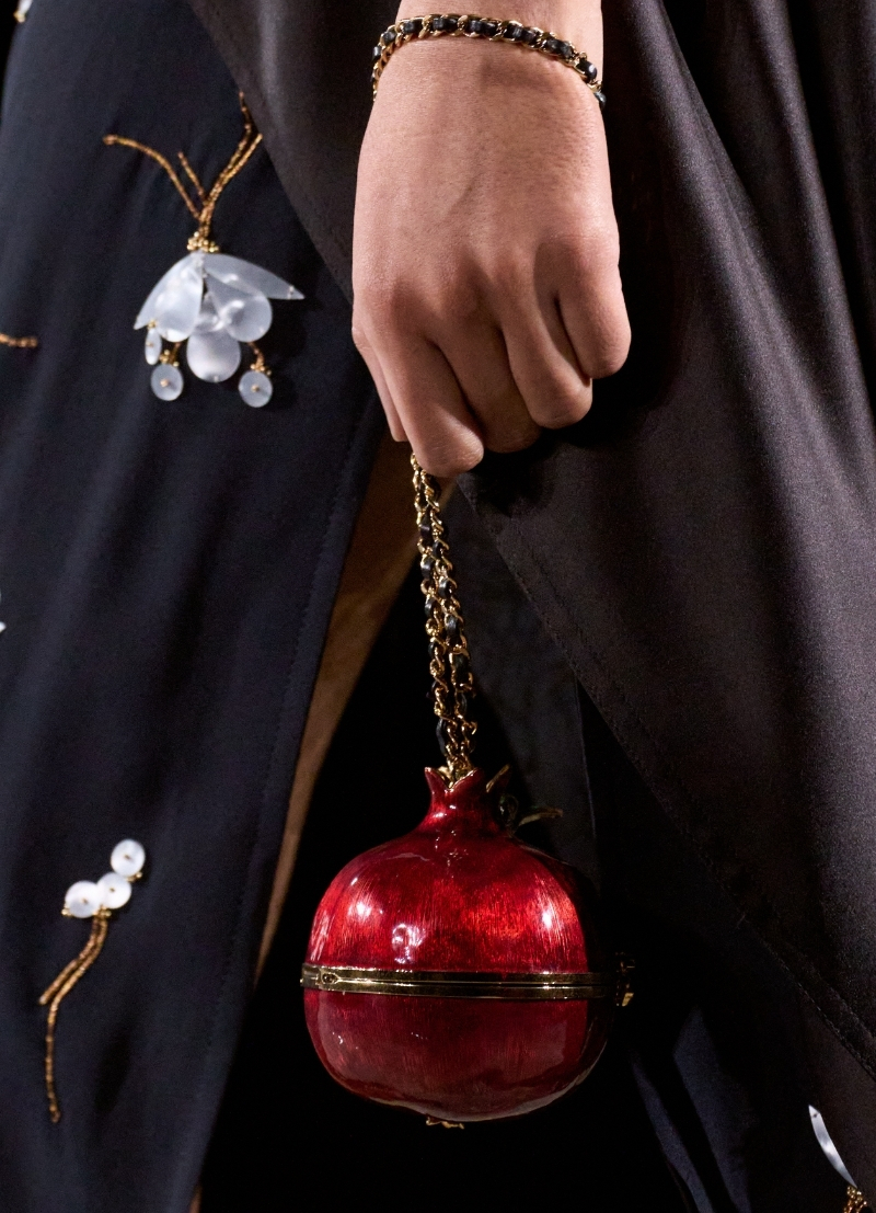 Red pomegranate-shaped evening bag with gold chain handle, styled against an embellished black runway dress