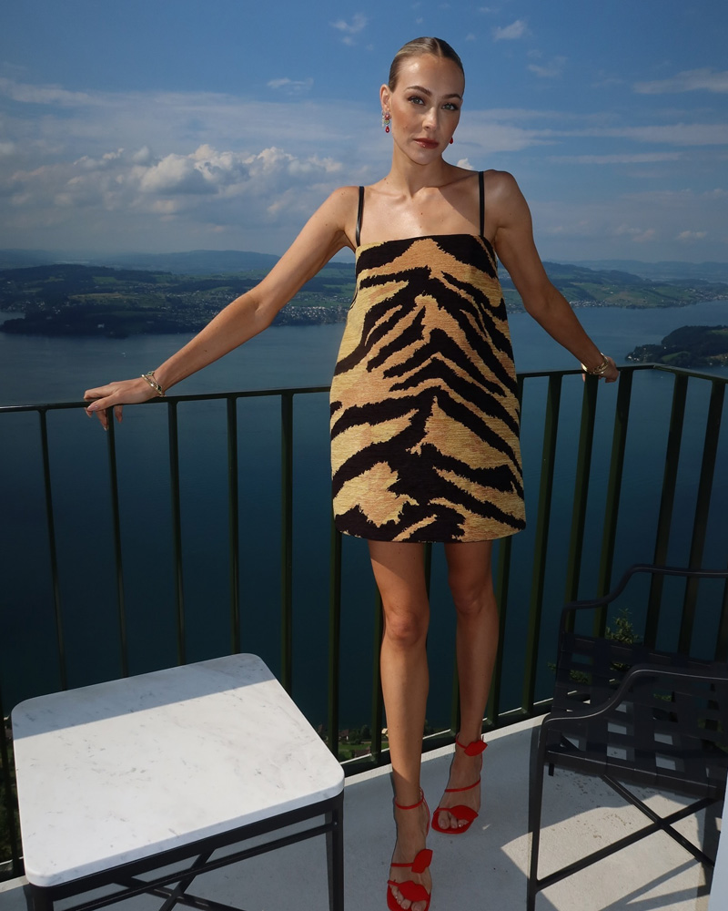 Tiger-print mini dress with thin straps and red heeled sandals styled on a scenic lakeside balcony