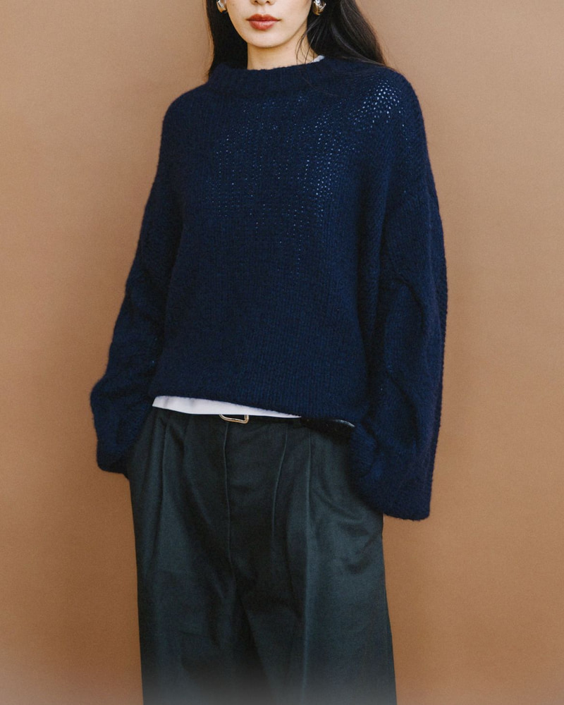 Model wearing a navy blue oversized knit sweater with balloon sleeves paired with high-waisted black trousers and gold hoop earrings