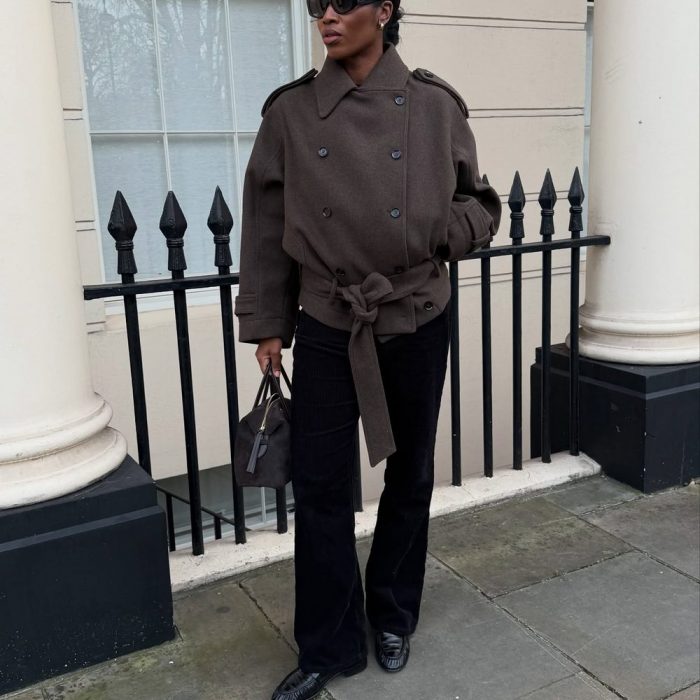 Chic winter outfit featuring a brown belted double-breasted coat, paired with black corduroy trousers and sleek leather loafers, styled with a mini bag and sunglasses.