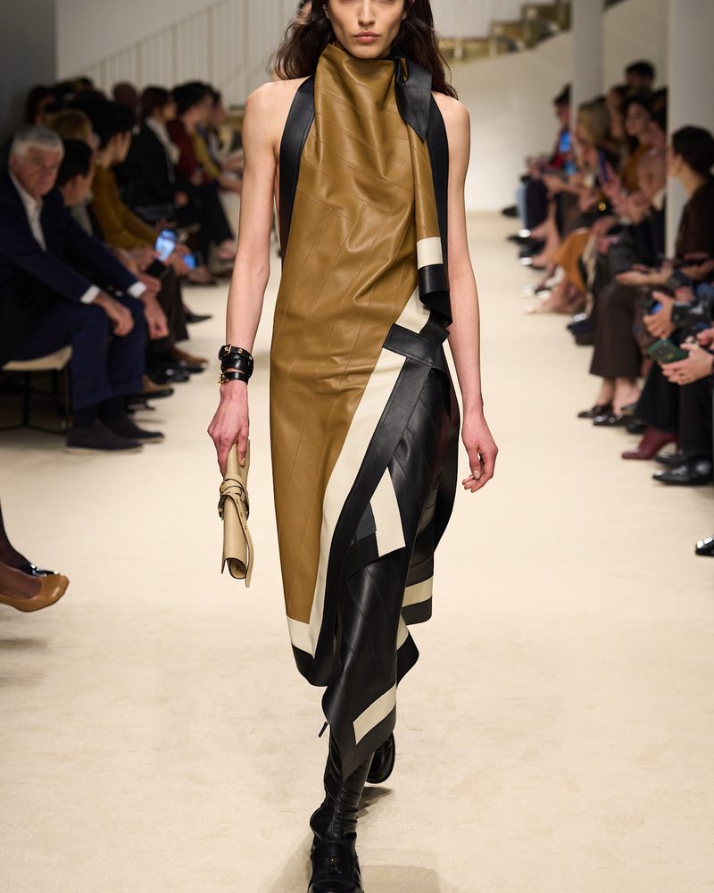 Sleek Tod%27s leather dress featuring a rich brown hue and geometric panels%2C accessorized with a minimalist beige clutch and stylish ankle boots