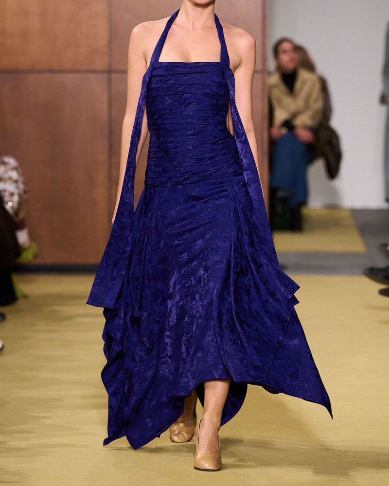 Model wearing a Tory Burch deep blue halter neck dress with textured fabric and asymmetrical hem on runway