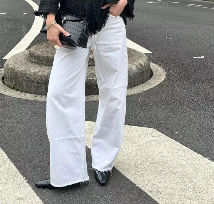 Chic black fringe jacket paired with high-waisted white wide-leg jeans, complemented by sleek black pointed-toe heels and a textured mini handbag.