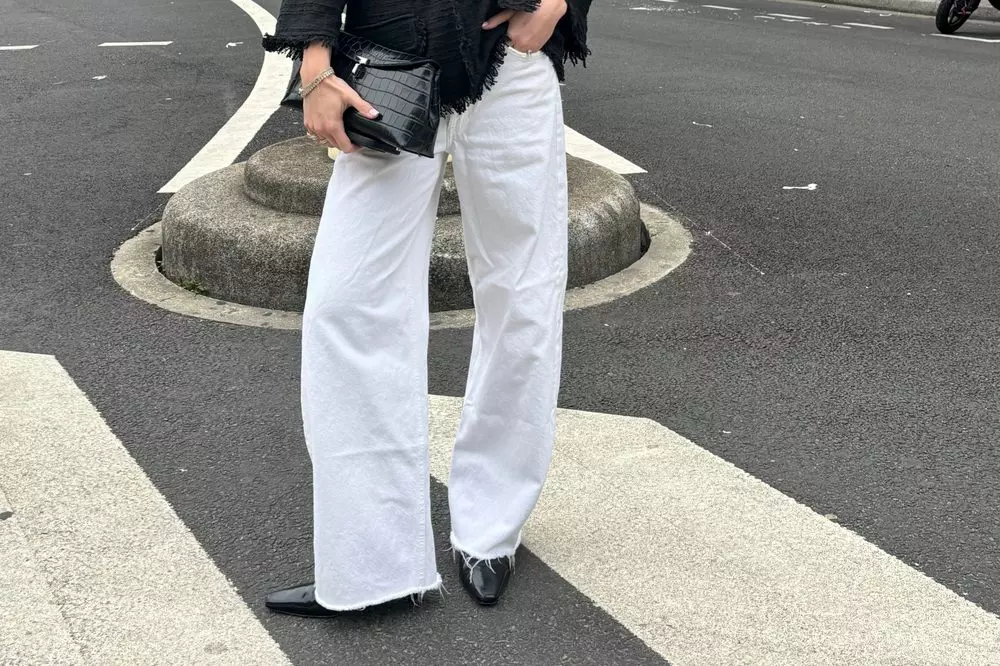 Chic black fringe jacket paired with high-waisted white wide-leg jeans, complemented by sleek black pointed-toe heels and a textured mini handbag.