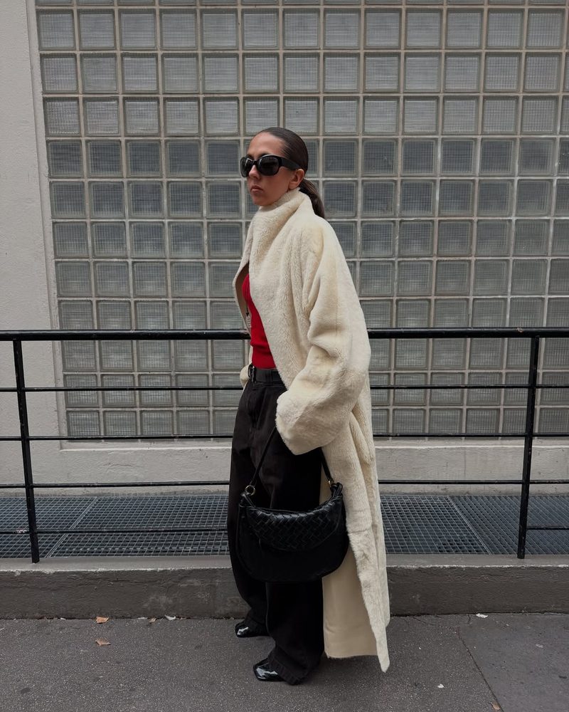 Chic winter outfit featuring a cozy cream faux fur coat over a red top%2C paired with black wide-leg trousers and a stylish black hobo bag.