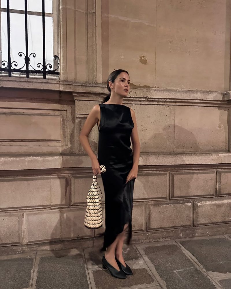 Sleek%2C black satin maxi dress with a high slit%2C paired with a woven cream handbag and black block-heeled shoes%2C exuding evening elegance