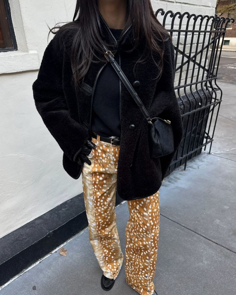 Chic winter ensemble featuring a cozy black teddy coat%2C a fitted black sweater%2C and bold earthy-toned wide-leg patterned pants with splashes of white