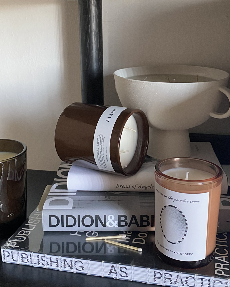 Luxury candle display featuring brown glass jars on stacked books%2C including D.S. %26 Durga and Nette scents%2C styled on a modern black shelf