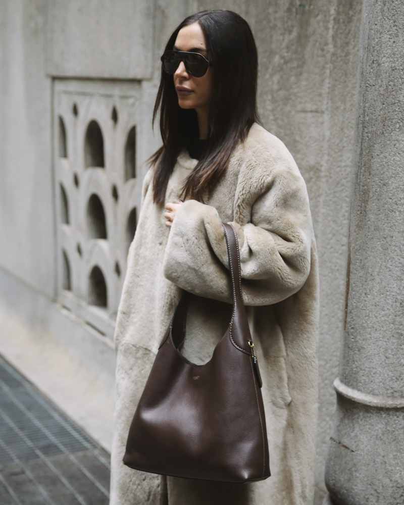 Winter street style featuring an oversized beige fur coat and dark brown leather Coach shoulder bag%2C paired with black sunglasses in a city backdrop