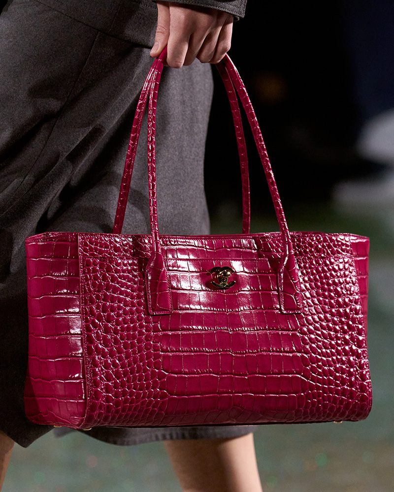 Chanel crocodile-embossed leather tote bag in deep red with gold CC turn-lock%2C styled with tailored skirt on runway backdrop