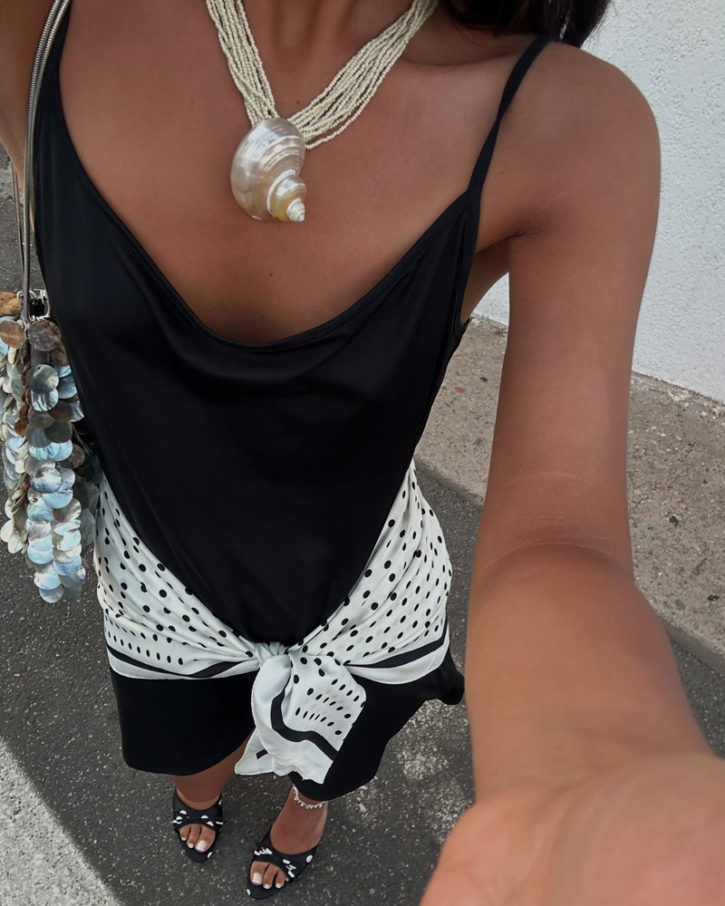 Black satin camisole styled with a black-and-white polka dot silk sarong%2C shell necklace and embellished bag on a sunny street