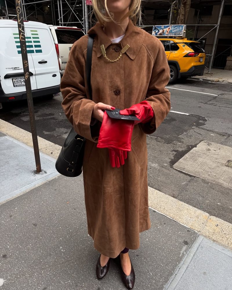 Chic street style look featuring a suede brown coat%2C vibrant red gloves%2C and elegant dark loafers%2C complemented by a black handbag.
