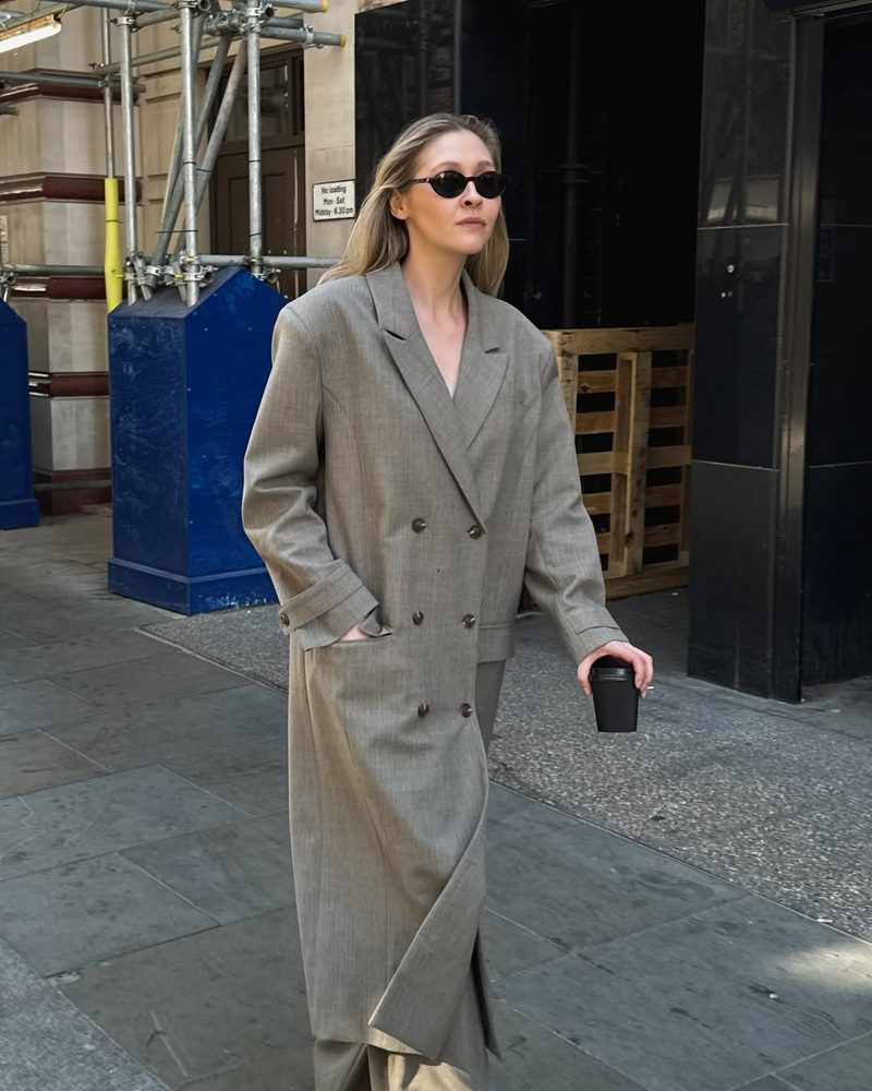 Gray oversized double-breasted coat with wide lapels%2C paired with sleek black sunglasses and a coffee cup%2C exuding modern elegance.