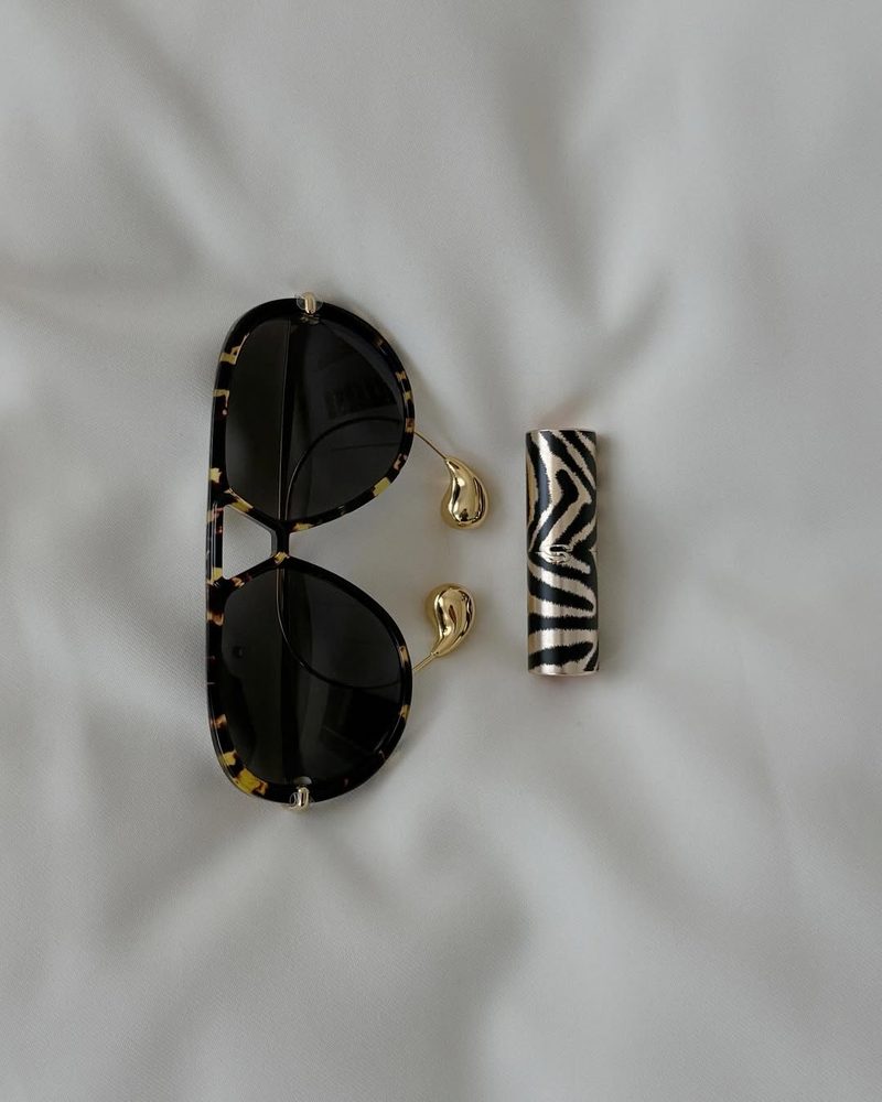 Tortoiseshell sunglasses with gold accents along with a chic zebra-striped lipstick%2C perfect summer essentials by Sisley Paris