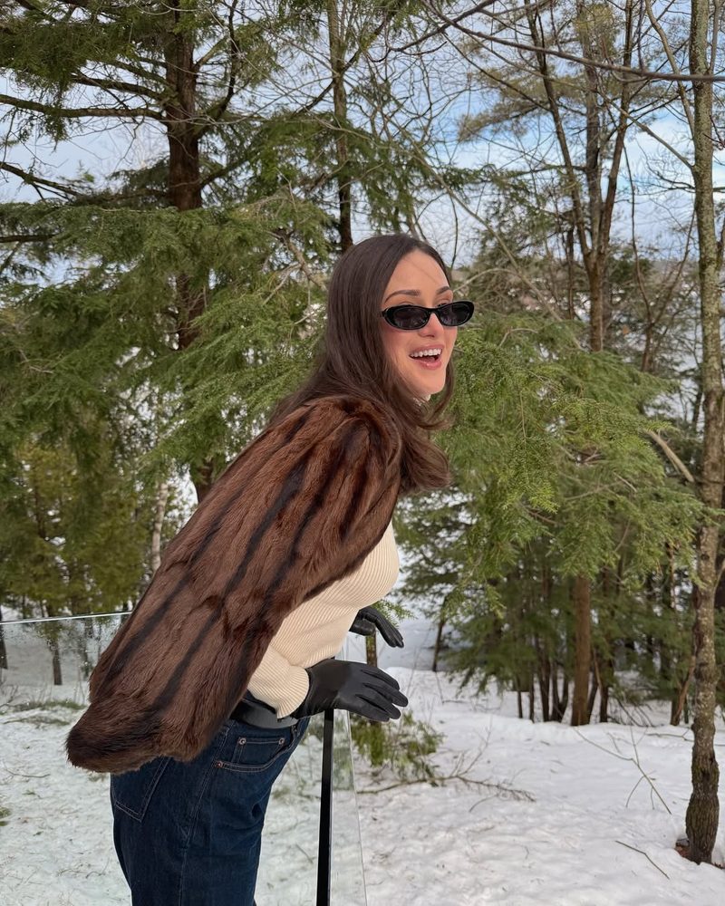 Chic winter outfit featuring a brown faux fur shawl layered over a cream sweater%2C paired with black leather gloves and dark denim jeans.