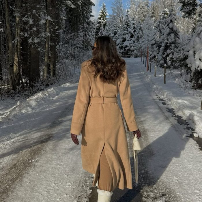 Classic beige wool coat with a belted waist paired with a cozy tan dress and white chunky boots, perfect for winter in the Dolomites