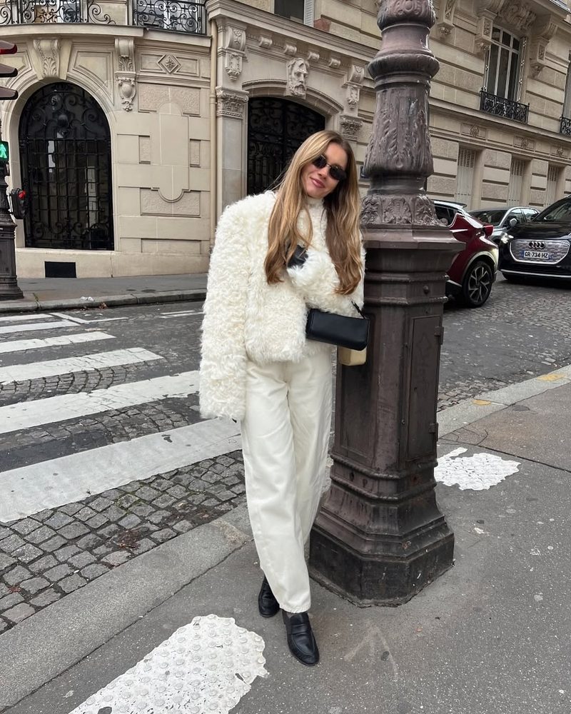 Cozy winter outfit featuring a fluffy white cropped jacket%2C cream wide-leg trousers%2C and sleek black ankle boots%2C styled with a chic black bag
