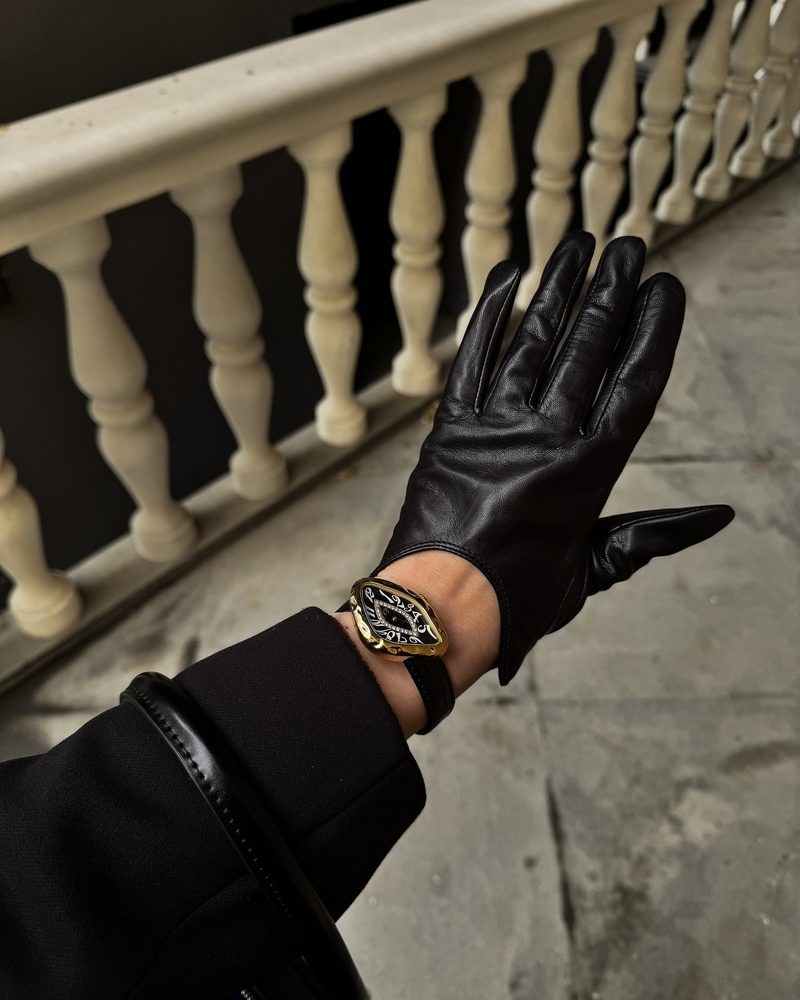 Sleek black leather gloves complement a sophisticated outfit%2C featuring a stylish timepiece with a gold bezel%2C perfect for winter elegance