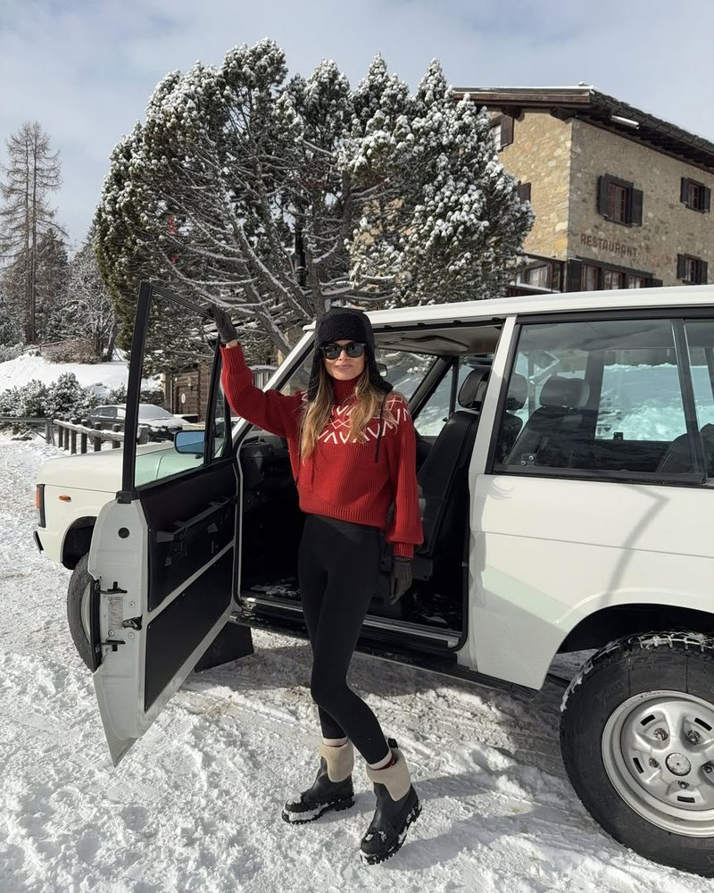 A cozy red knit sweater with geometric patterns paired with black leggings and stylish black snow boots%2C set against a snowy backdrop.