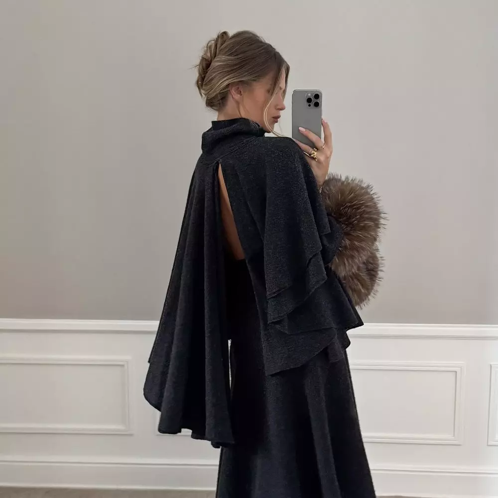 Elegant black winter work dress with a dramatic cape overlay, featuring a back cutout, styled with strappy heels and a chic fur clutch