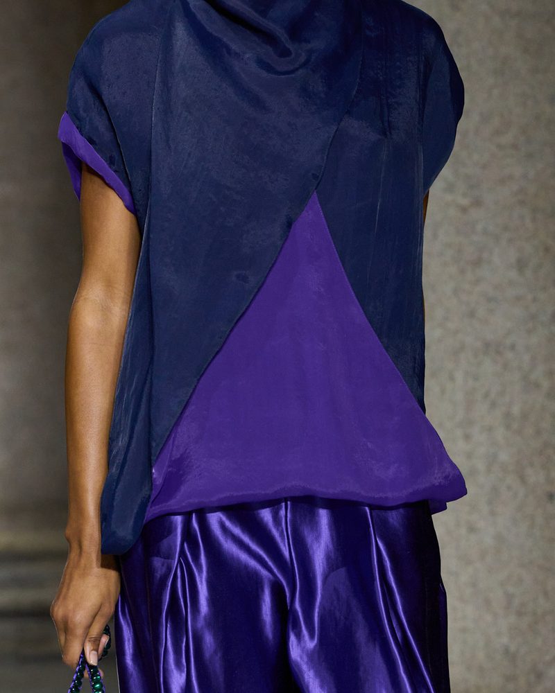 Giorgio Armani ensemble showcases a layered purple and navy silk top paired with shiny satin trousers%2C highlighting modern elegance.
