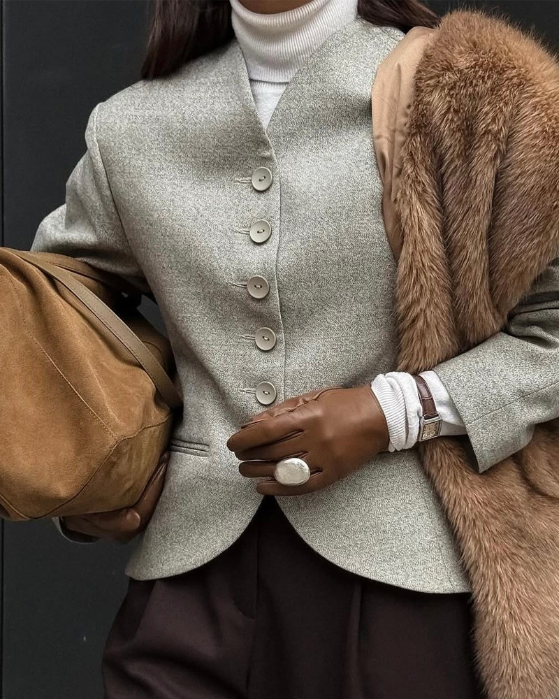 Close-up of a gray wool vest layered over a white turtleneck with leather gloves%2C suede bag%2C and fur stole in a city setting