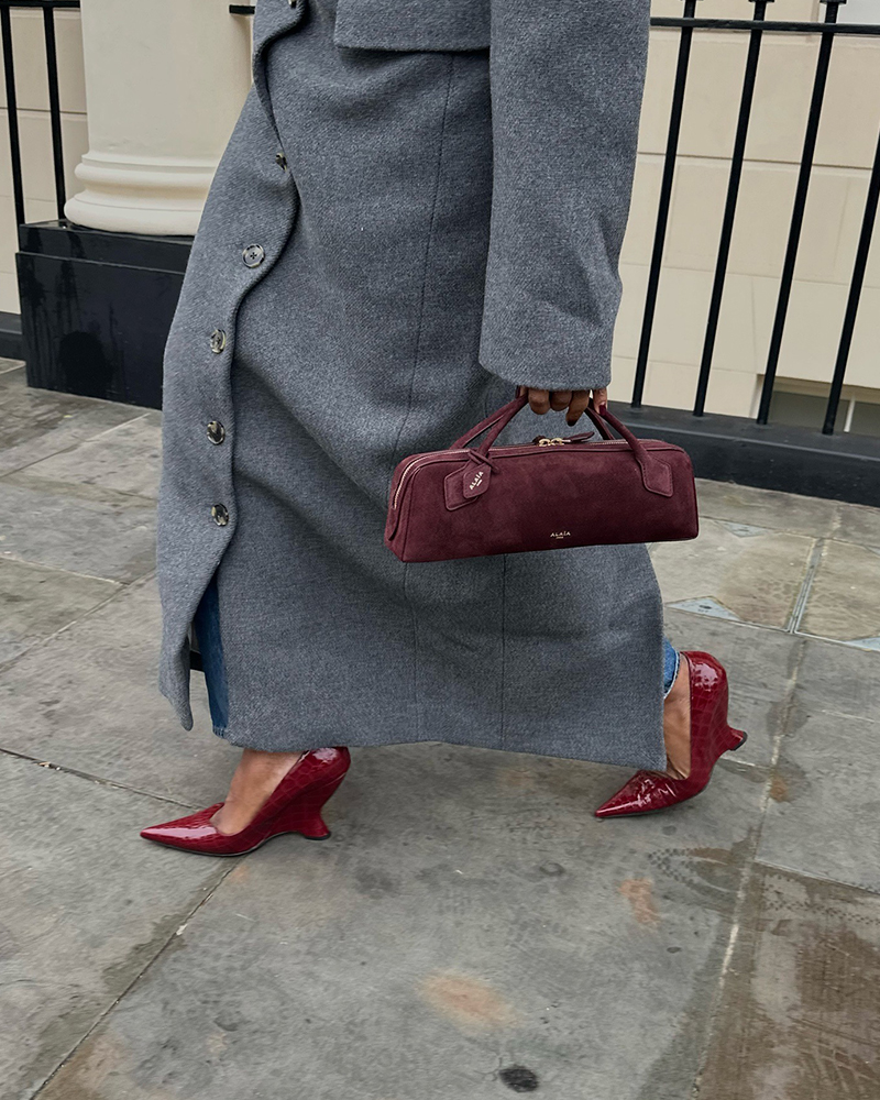 Ala%C3%AFa burgundy suede bag paired with a gray wool coat and burgundy pointed heels on a city sidewalk